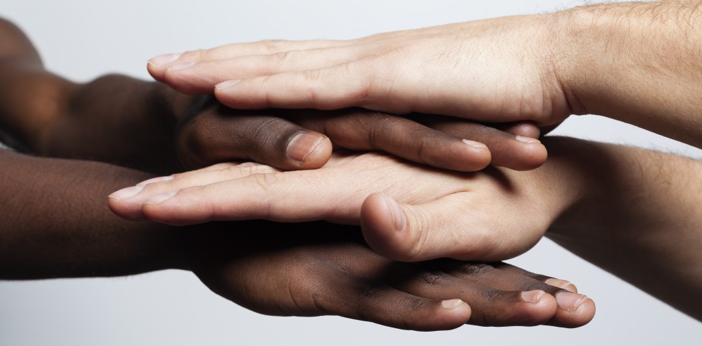 Multiracial hands together forming a pile over gray background ...